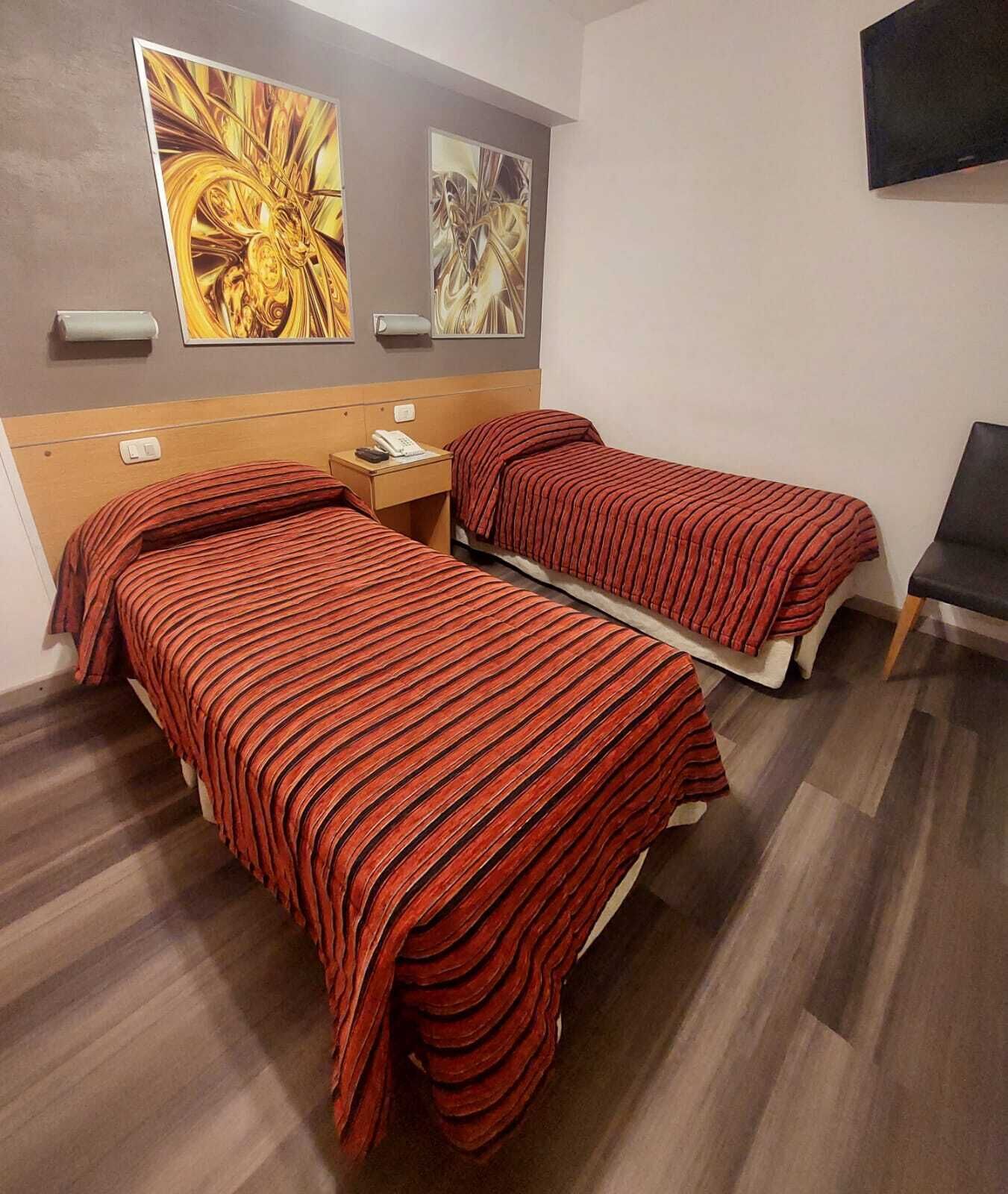 Quarto de hotel com duas camas, cabeceira de madeira, televisão de tela plana na parede e obras de arte acima das camas.