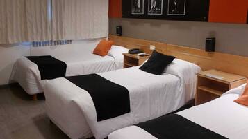 Quarto de hotel com três camas de solteiro, cabeceira de madeira, ar-condicionado fixado na parede e janela com cortinas.