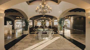 Um hall amplo com um imponente candelabro, tetos abobadados e uma mesa redonda central.