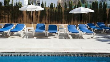 Uma área à beira da piscina com espreguiçadeiras azuis e guarda-sóis brancos.