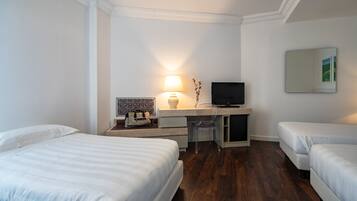 Quarto de hotel com duas camas, uma mesa de trabalho com uma televisão, um abajur e um espelho na parede.