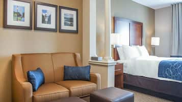 Quarto de hotel com sofá de couro marrom, um banquinho combinando, cama com roupa de cama branca e três quadros na parede.