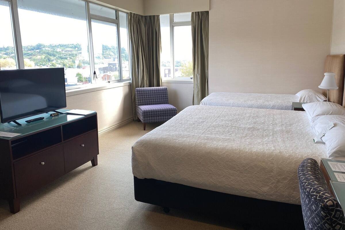 Quarto de hotel com duas camas, uma televisão, uma escrivaninha e uma cadeira.