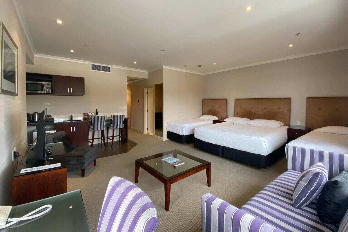 Quarto de hotel com duas camas de solteiro, um sofá, uma mesa de centro, uma televisão e uma kitchenette.