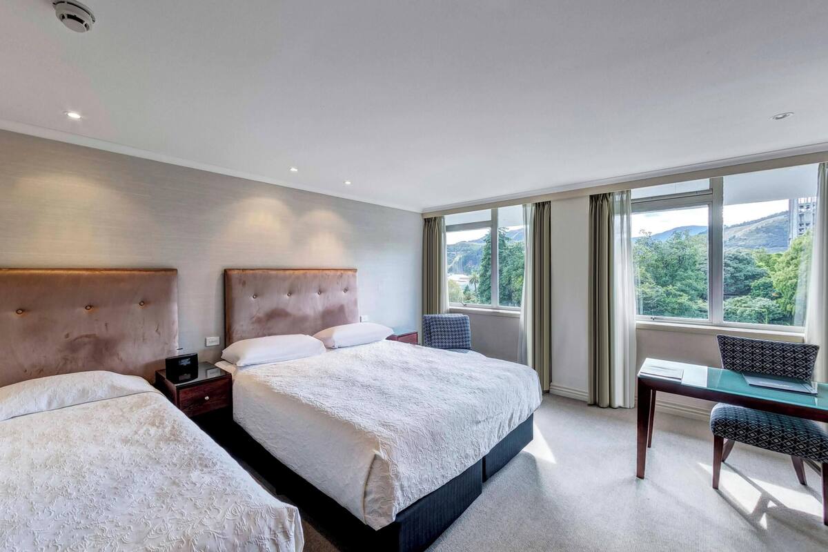 Quarto de hotel com duas camas, uma escrivaninha e vista para o exterior.