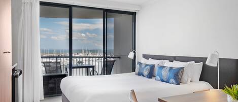 Quarto de hotel com uma cama grande, uma escrivaninha, uma cadeira e uma varanda com vista para o porto de iates.