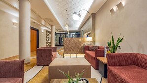 Um lobby moderno com área de estar central, balcão de recepção e teto trabalhado.