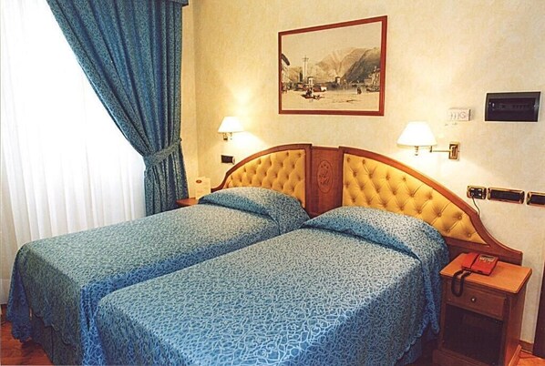 Quarto de hotel com duas camas, cabeceira de madeira, quadro na parede e mesa de cabeceira com abajur.