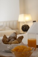 Uma mesa com um café da manhã, incluindo pães, um copo de suco de laranja e uma tigela de frutas.