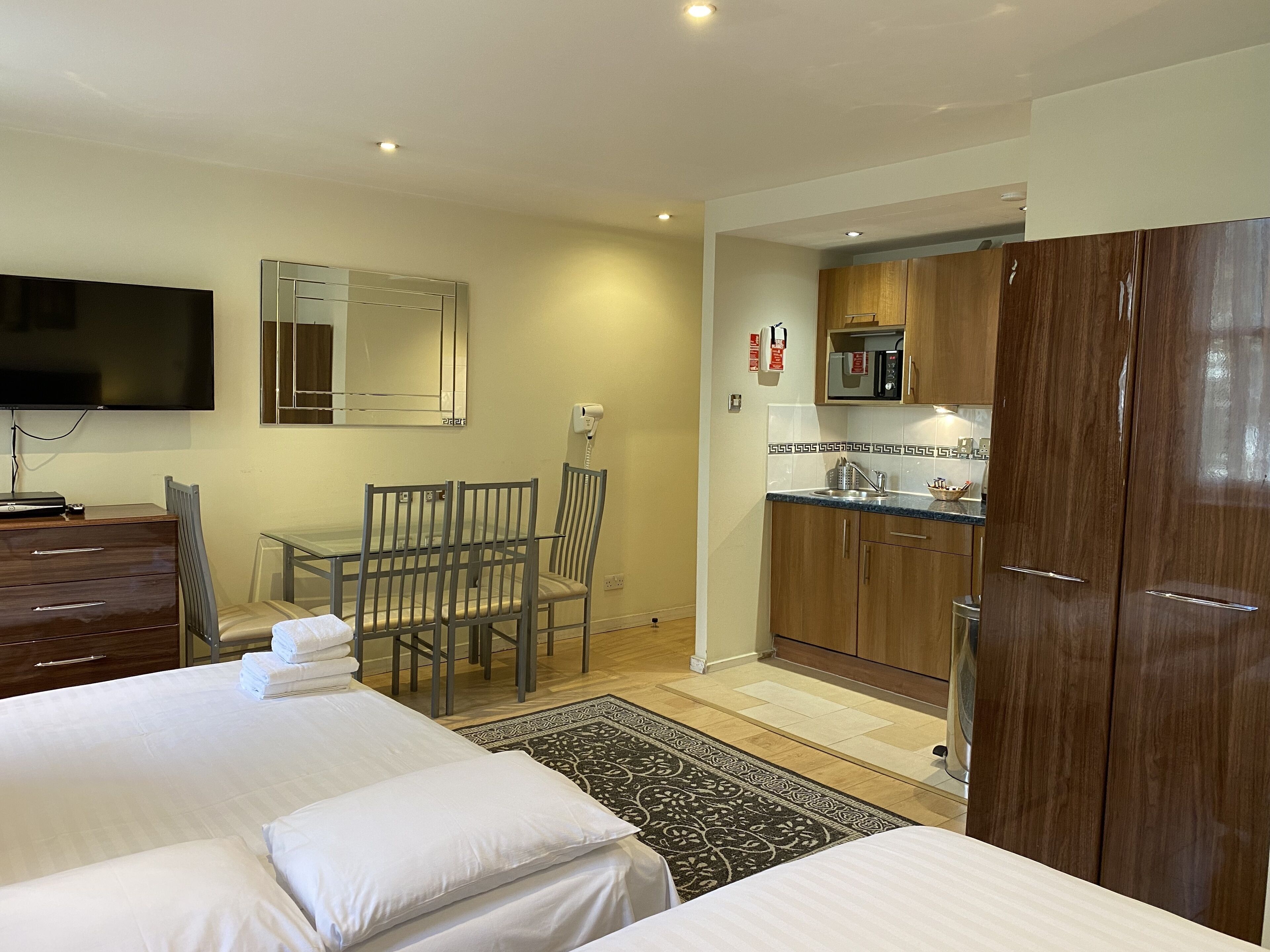 Quarto de hotel com cama, escrivaninha, cadeira, televisão, micro-ondas e armários de madeira.