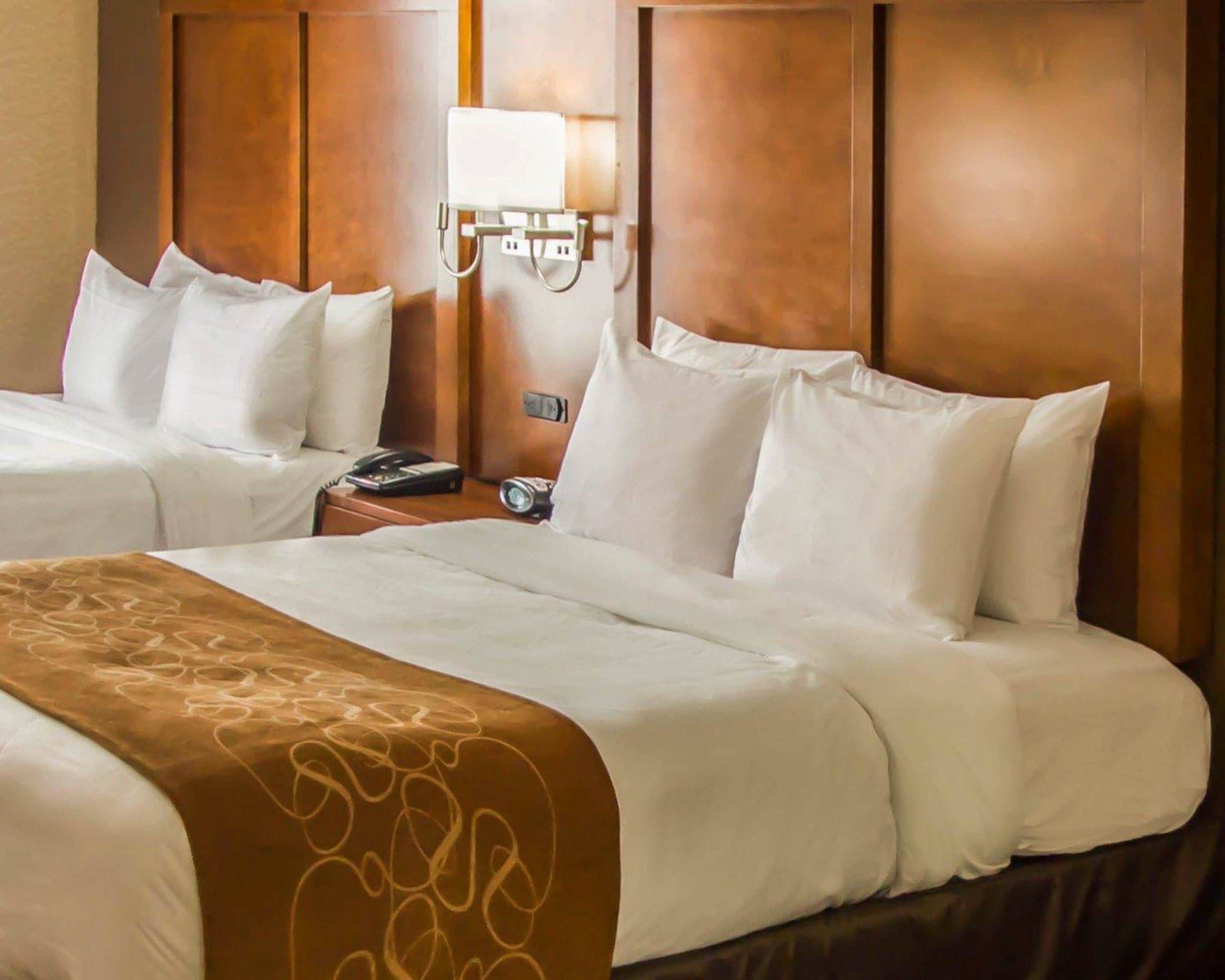 Quarto de hotel com duas camas, uma mesa de cabeceira com abajur e um telefone.