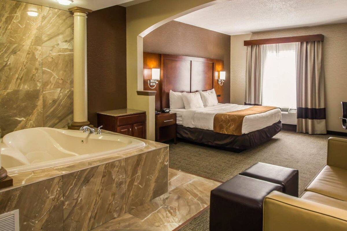 Quarto de hotel com banheiro amplo em mármore, cama king-size, área de estar e vista da cidade.