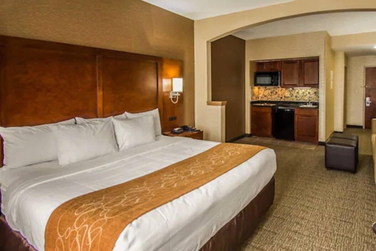 Quarto de hotel com cama grande, cozinha compacta e banheiro separado.