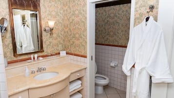 Uma casa de banho com um espelho grande, uma pia com artigos de higiene, uma sanita e um roupeiro pendurado na parede.