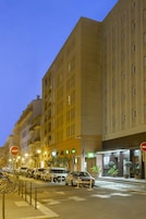 Hotel com vários andares, varandas, área de estacionamento e vista para a rua.