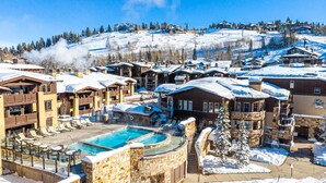 Um resort com área de piscina, vários edifícios e uma montanha nevada ao fundo.