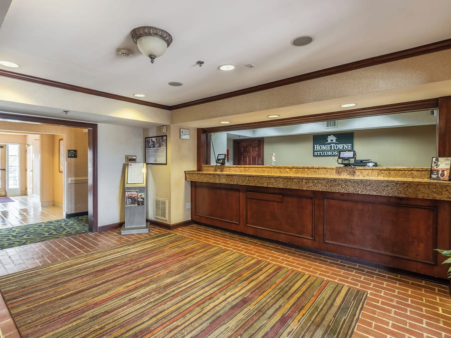 Uma área de recepção de hotel com balcão, tela digital e placa da HomeTowne Studios.