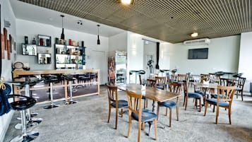 Restaurante com interior moderno, com mesas e cadeiras de madeira, área de bar e teto com padrão único.