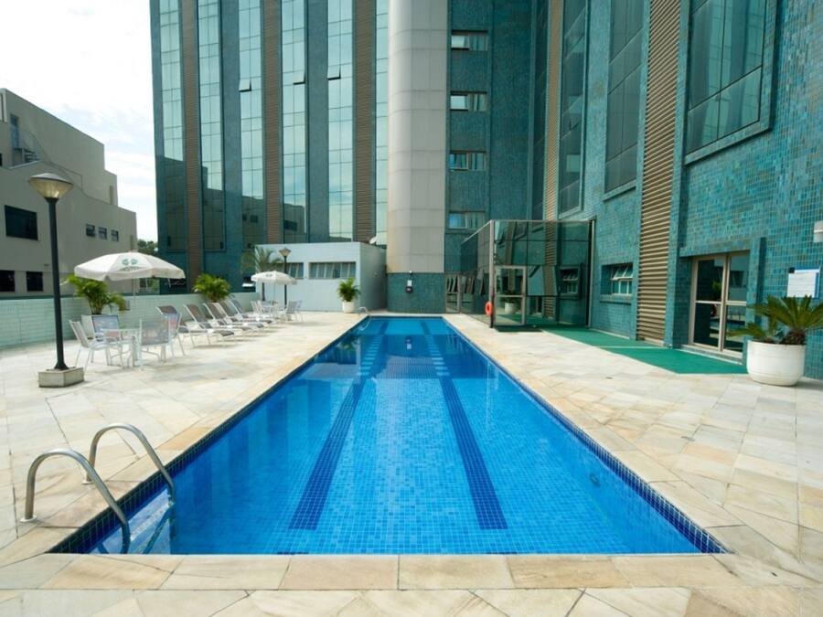 Piscina com espreguiçadeiras e guarda-sóis, rodeada por edifícios modernos.