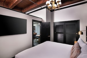 Quarto de hotel moderno com uma cama grande, televisão de tela plana na parede e uma porta de madeira escura.