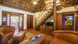 Uma sala de estar ampla, com teto alto, escada de madeira e uma televisão sobre um armário de madeira.