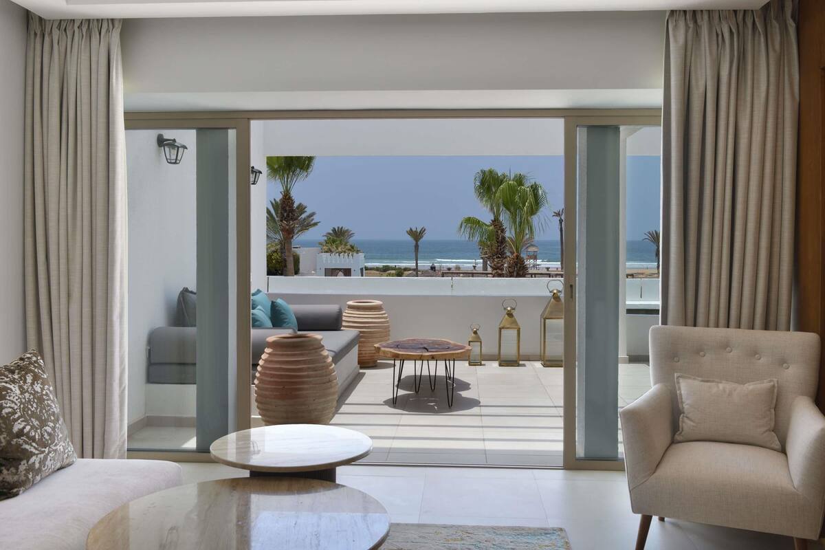 Uma sala de estar moderna com vista para a praia, um sofá, uma mesa de centro redonda e uma cadeira.