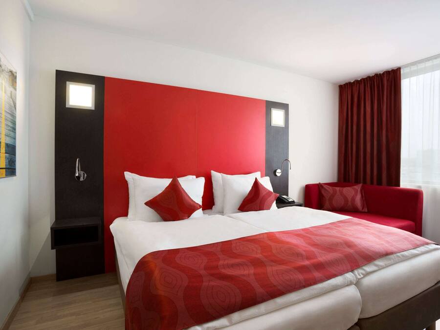 Quarto de hotel com uma cama grande, um sofá vermelho e um quadro na parede.