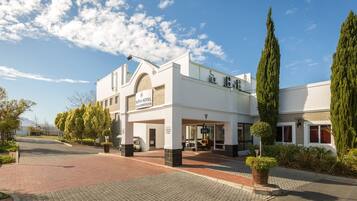 Um hotel com design arquitetônico moderno, destacando uma entrada imponente, área de estacionamento e um jardim bem cuidado com vasos de plantas.