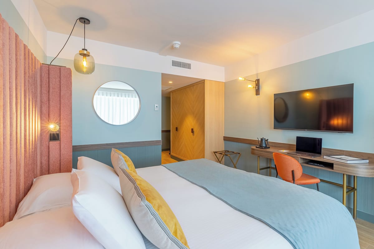 Quarto de hotel moderno com uma cama grande, uma escrivaninha com um laptop, uma televisão e um espelho.