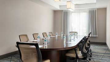 Uma sala de conferências com uma mesa comprida, seis cadeiras e garrafas de água sobre a mesa.