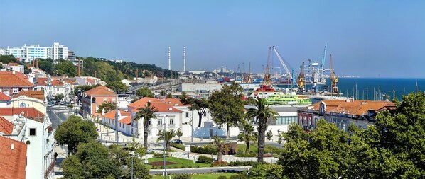 Paisagem costeira com edifícios, um porto com guindastes e um céu claro.