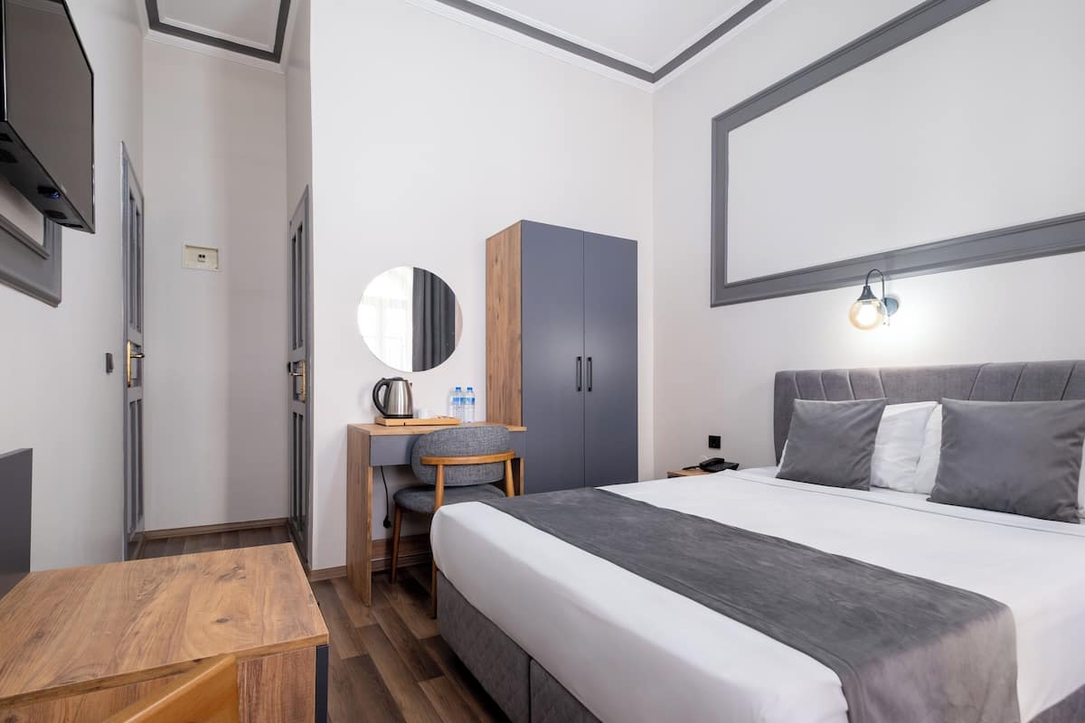 Quarto de hotel moderno com uma cama grande, uma escrivaninha com cadeira, um guarda-roupa e uma televisão.