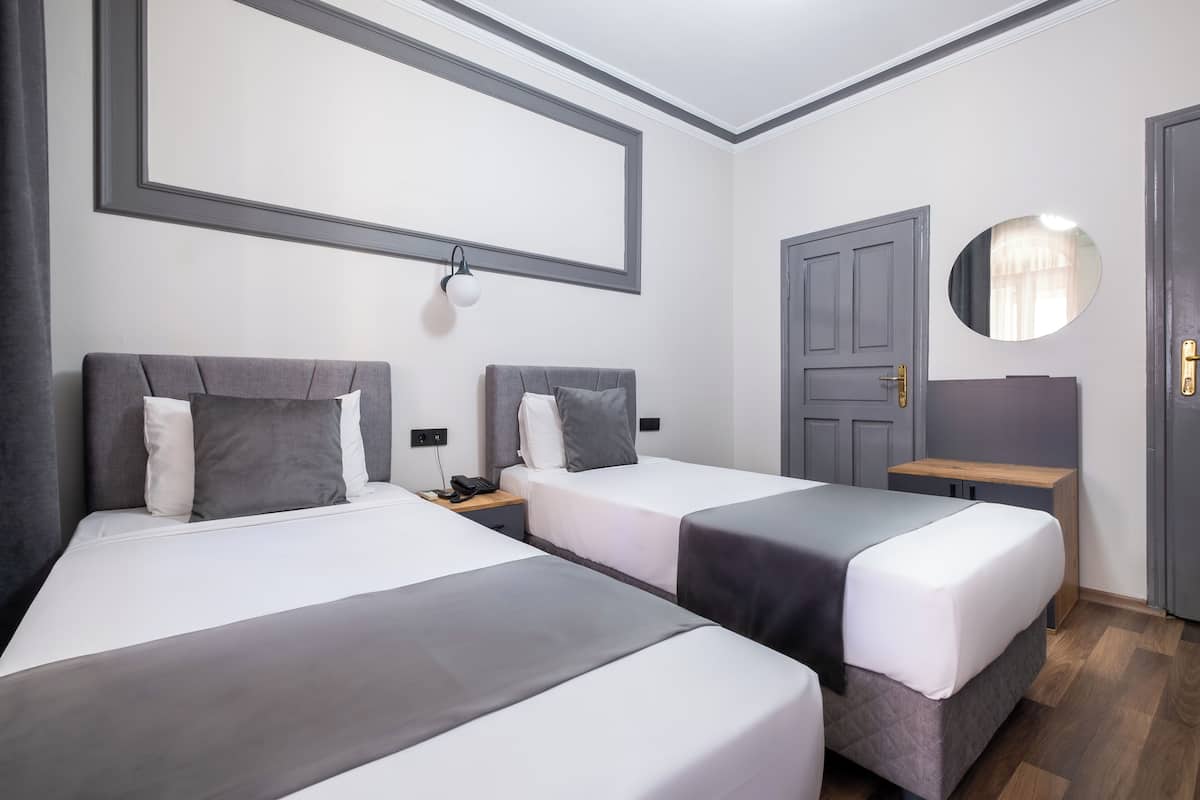 Quarto de hotel com duas camas, uma mesa de cabeceira com abajur, um espelho e uma porta.