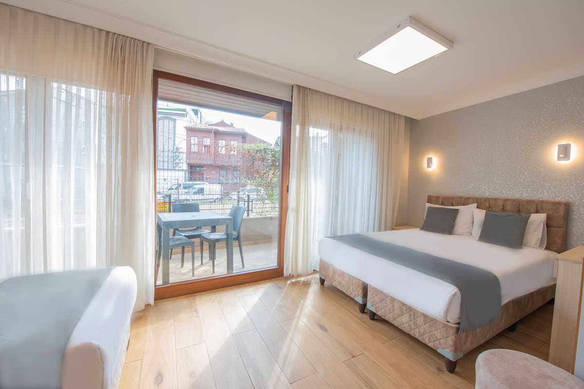 Quarto de hotel com cama grande, escrivaninha e varanda com mesa e cadeiras.