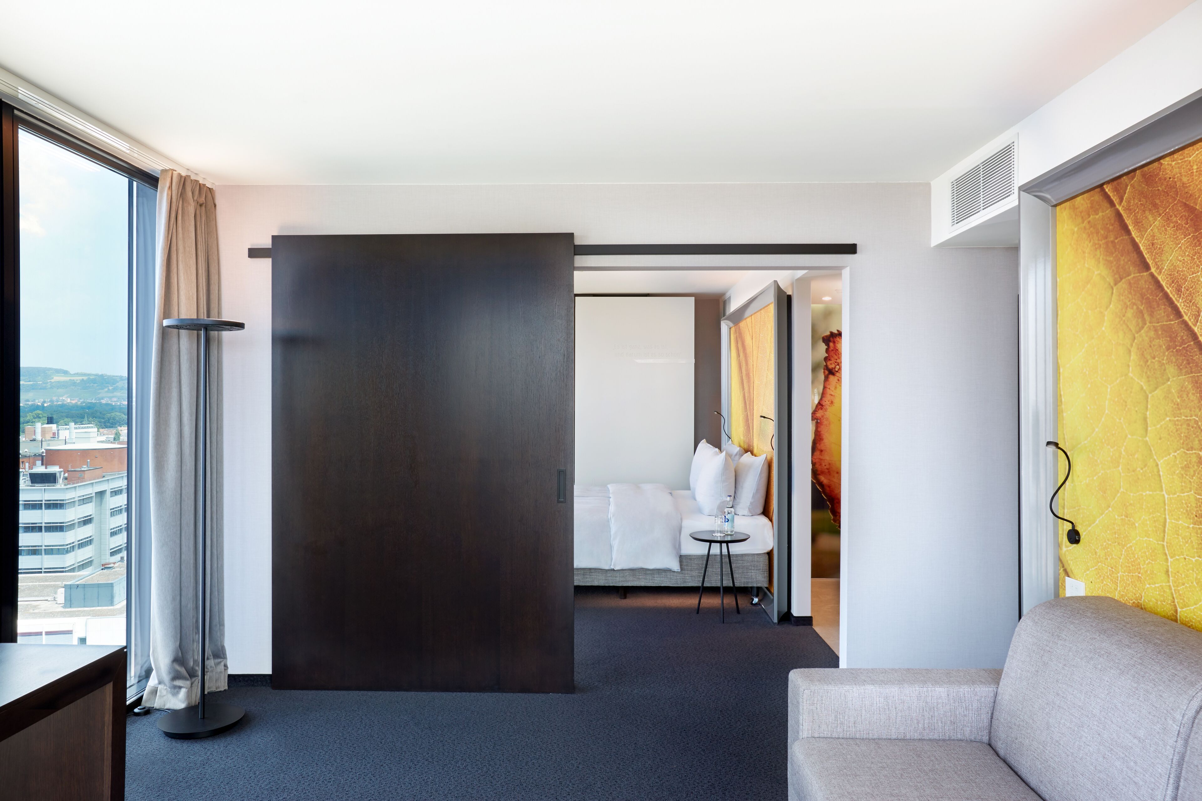 Quarto de hotel com uma janela grande, um sofá, uma cama e uma mesinha.