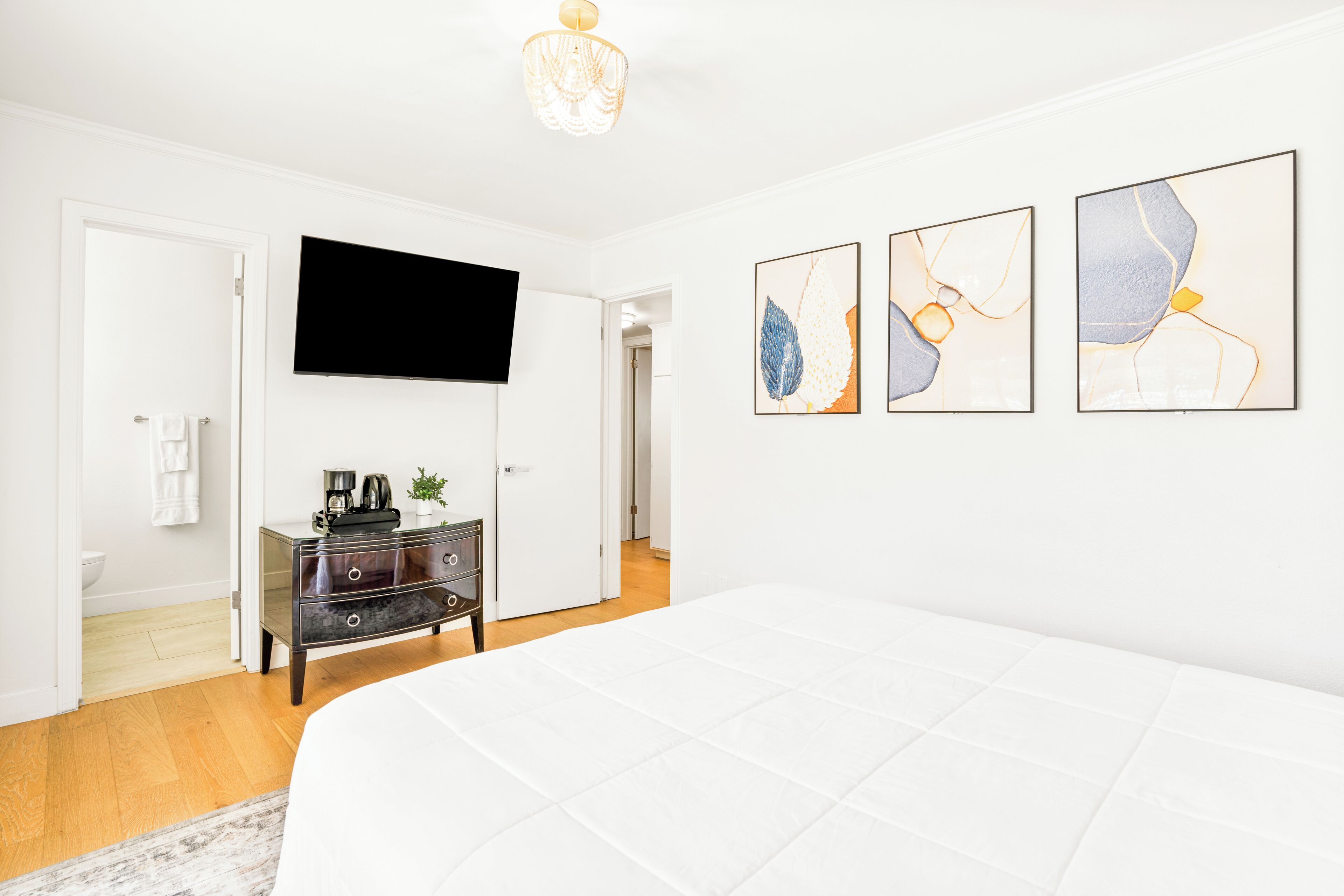 Quarto com uma cama grande, uma TV de tela plana na parede e três pinturas abstratas.