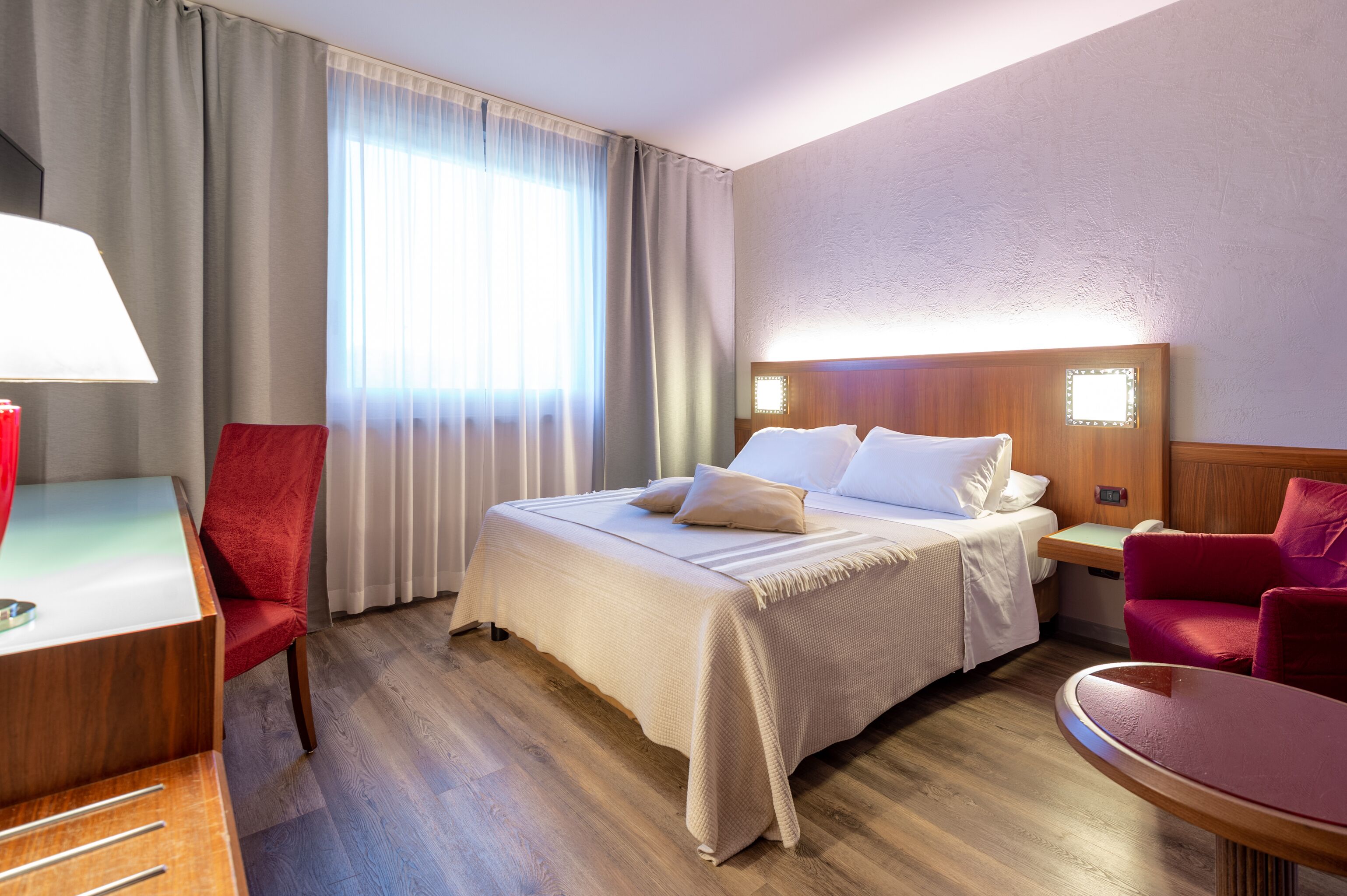 Quarto de hotel com cama, secretária, cadeira e mesa.
