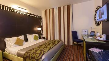 Quarto de hotel com uma cama grande, uma escrivaninha com um laptop, uma televisão e uma mala.