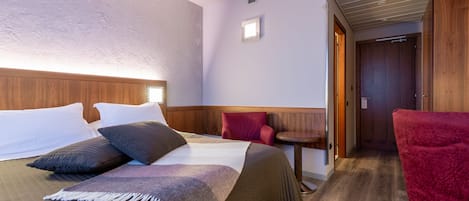 Quarto de hotel com uma cama grande, uma mesa pequena, uma cadeira vermelha e uma porta de madeira.