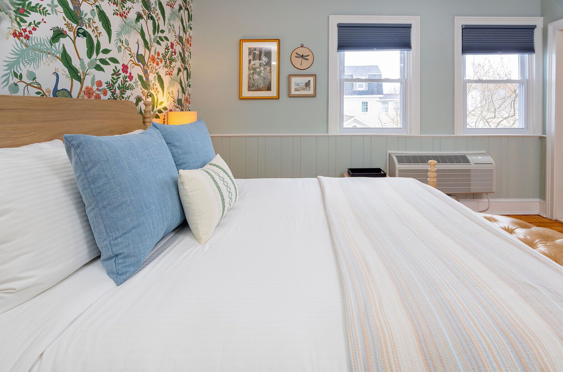 Quarto com cama, almofadas, parede com quadros e janelas com persianas.