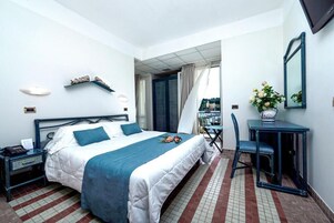 Quarto de hotel com cama, escrivaninha, cadeira, espelho e vista para o exterior.