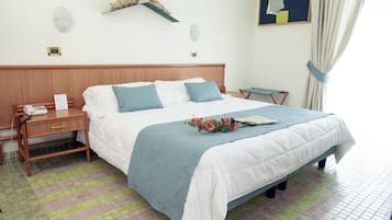 Uma cama bem arrumada com um edredom azul e branco, uma mesa de cabeceira com um telefone e um bloco de notas, e uma pequena mesa de cabeceira com uma luminária.