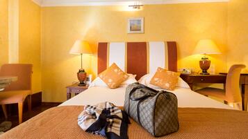 Quarto de hotel com cama, duas cadeiras, escrivaninha e abajur.