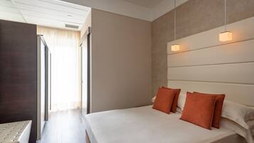 Quarto de hotel com uma cama, duas almofadas, mesa de cabeceira e janela com cortinas.