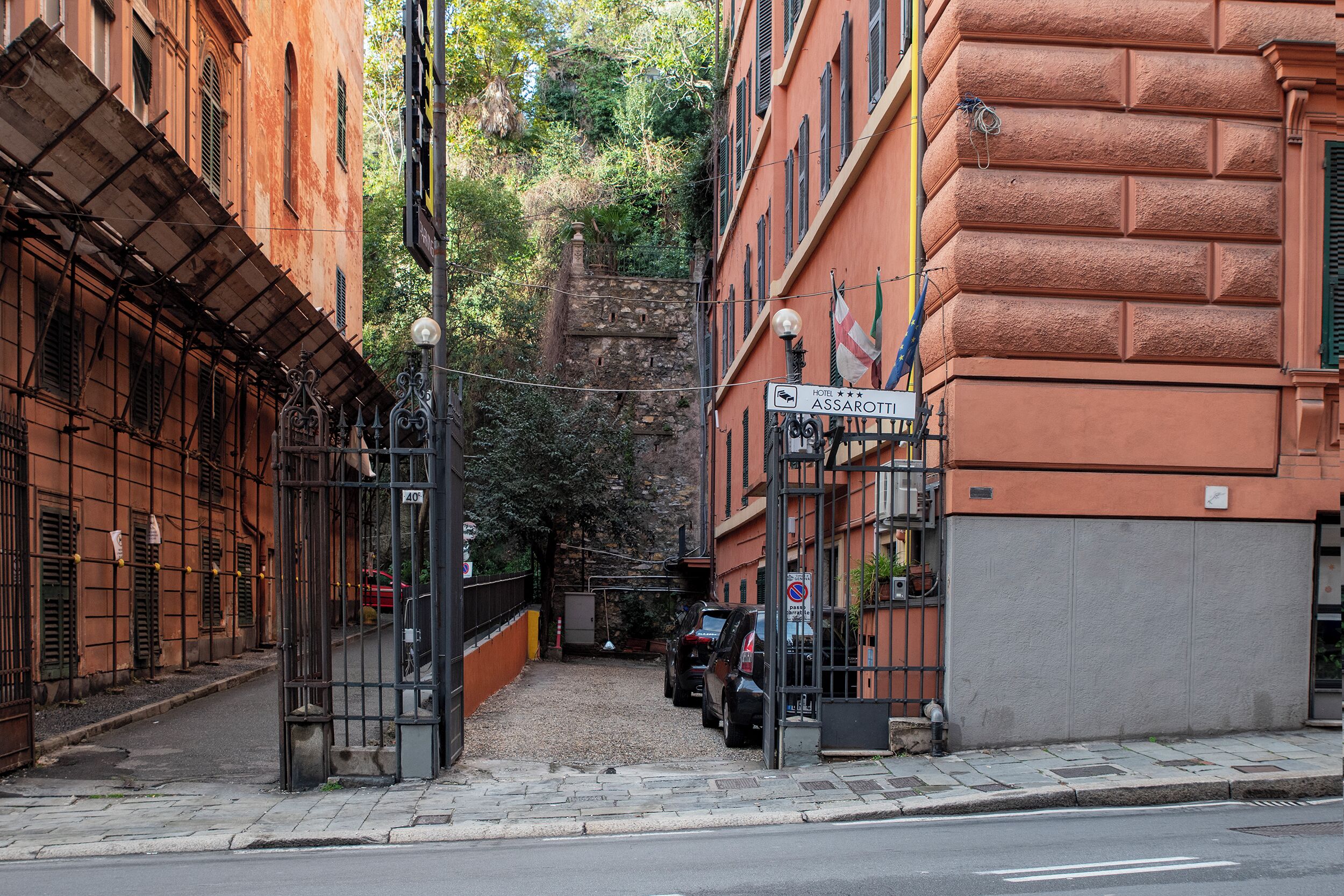 Rua estreita com carros estacionados e um edifício com a placa 'Hotel Assarotti'.