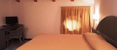 Quarto com cama, escrivaninha com computador e janela com cortinas.