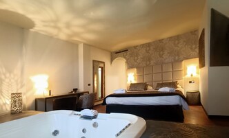 Quarto de hotel com uma banheira grande, duas camas com cabeceiras, abajures, um espelho e uma pequena escrivaninha.