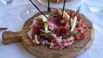 Tábua de madeira com fatias de carne e queijo, acompanhada por um copo de vinho rosé, sobre uma mesa com toalha branca.