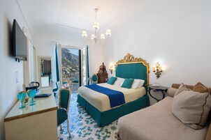Quarto de hotel com cama, escrivaninha, cadeira, televisão e varanda com vista para as montanhas.