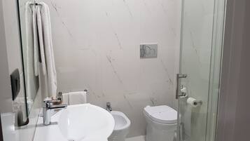 Uma casa de banho moderna com cabine de duche em vidro, lavatório branco, bidé e sanita.